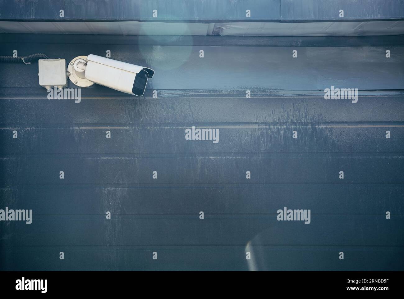 An outdoor video camera is mounted on a dirty metal wall. Security ...