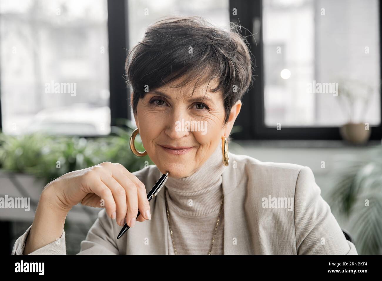 mature woman entrepreneur with pen looking at camera in office ...