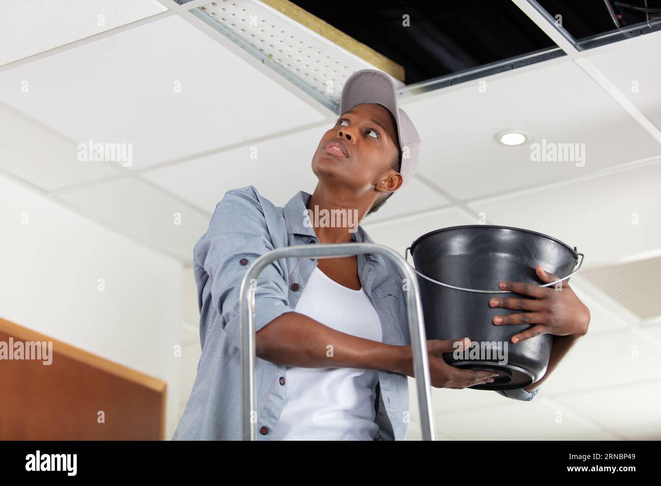 worried woman holding bucket while water droplets leaking from ceiling ...