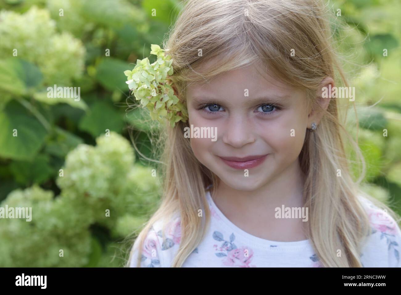 Candid outdoor portrait of happy little girl with green flower behind ...