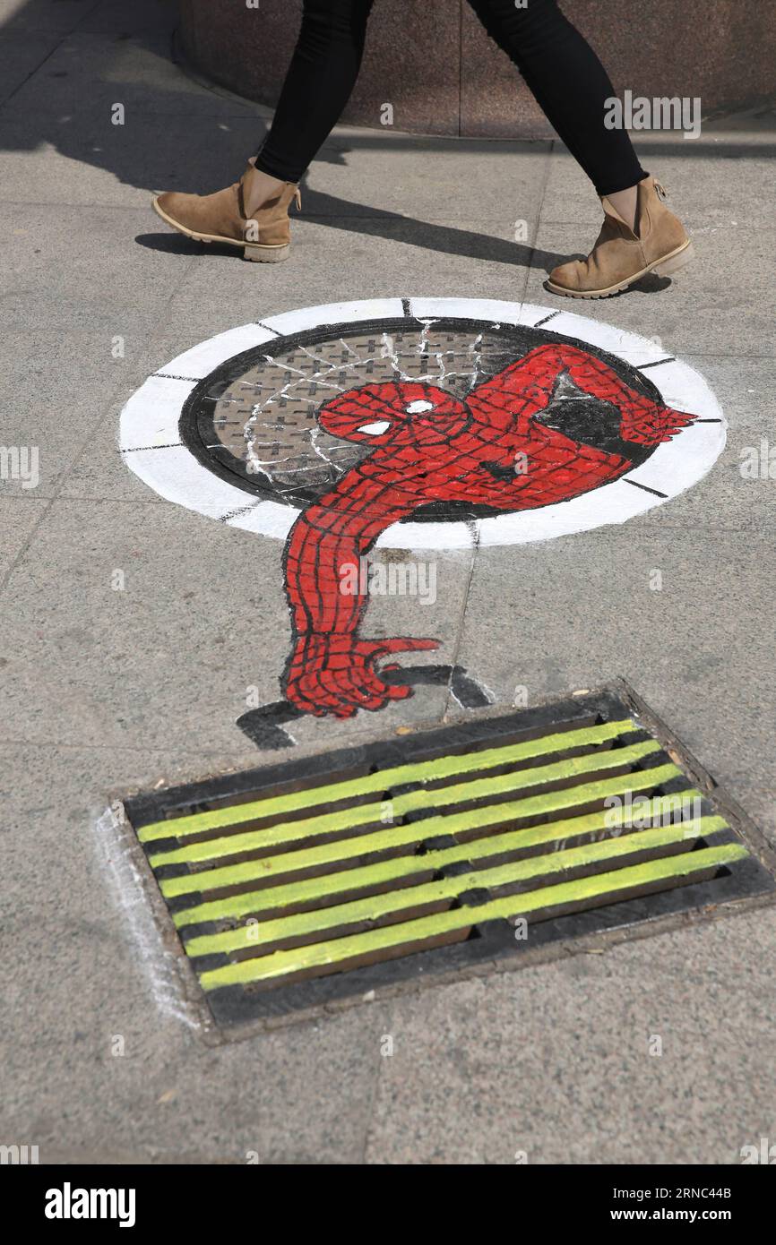People walk past a manhole cover, which is painted with a spider man at ...