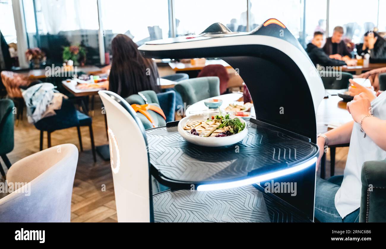 Robot waiter serve food at modern restaurant table.Offering innovation ...