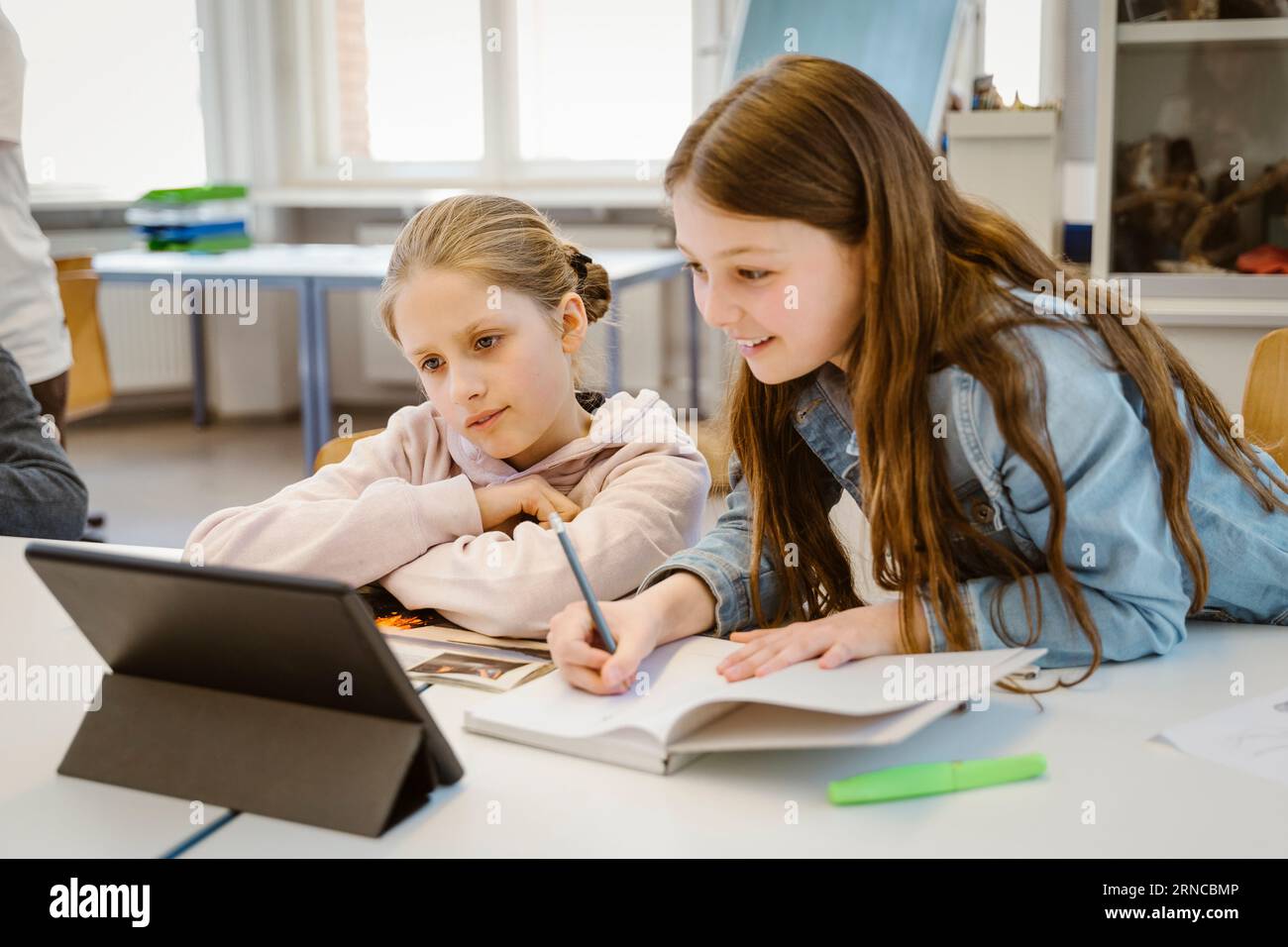 Curious schoolgirls doing E-learning through tablet PC sitting at desk ...