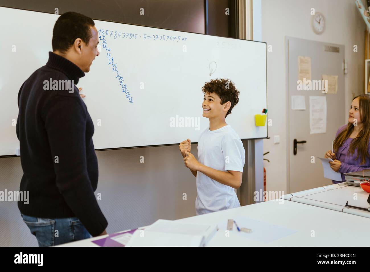 Smiling boy talking to male teacher standing near whiteboard in ...