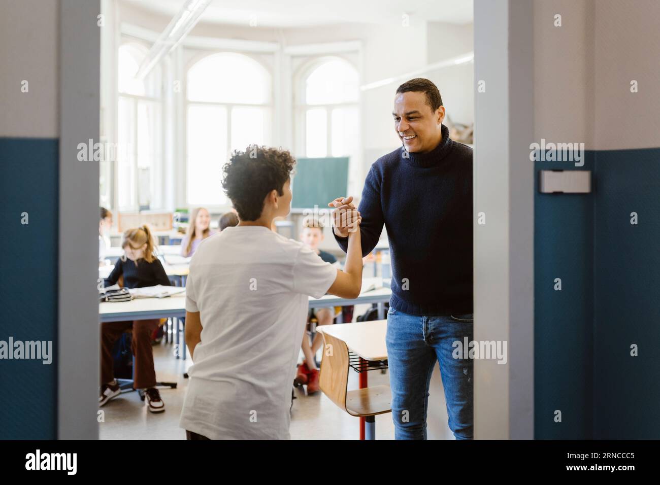 Smiling male teacher doing handshake with student in classroom Stock ...