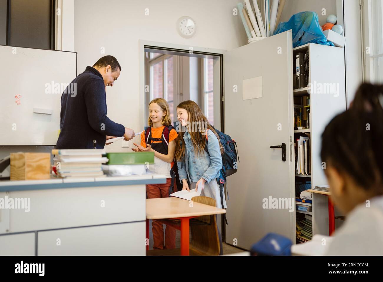 Mature male teacher giving documents to students standing in classroom Stock Photo - Alamy