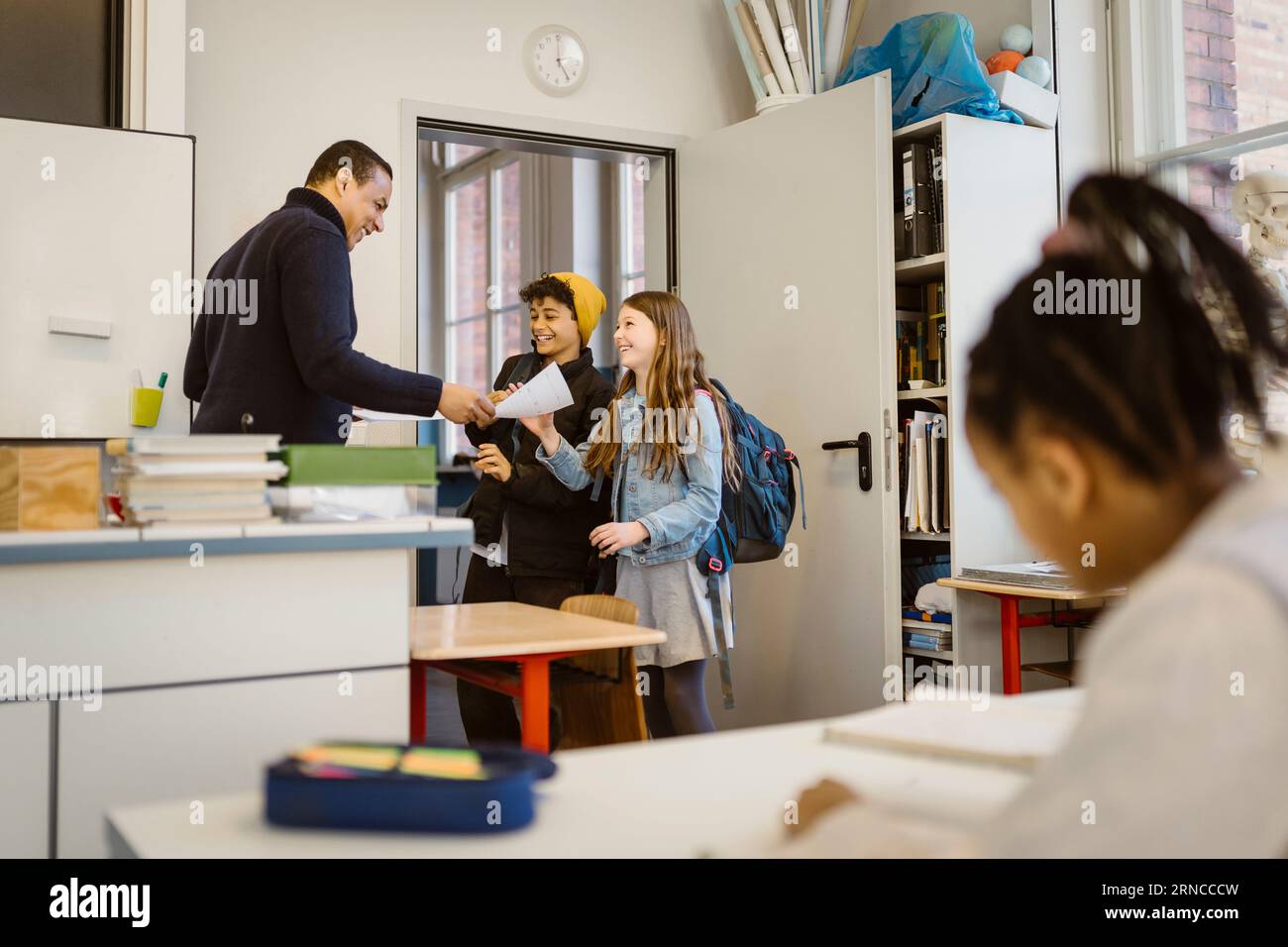 Mature male teacher giving documents to happy students standing in classroom Stock Photo - Alamy