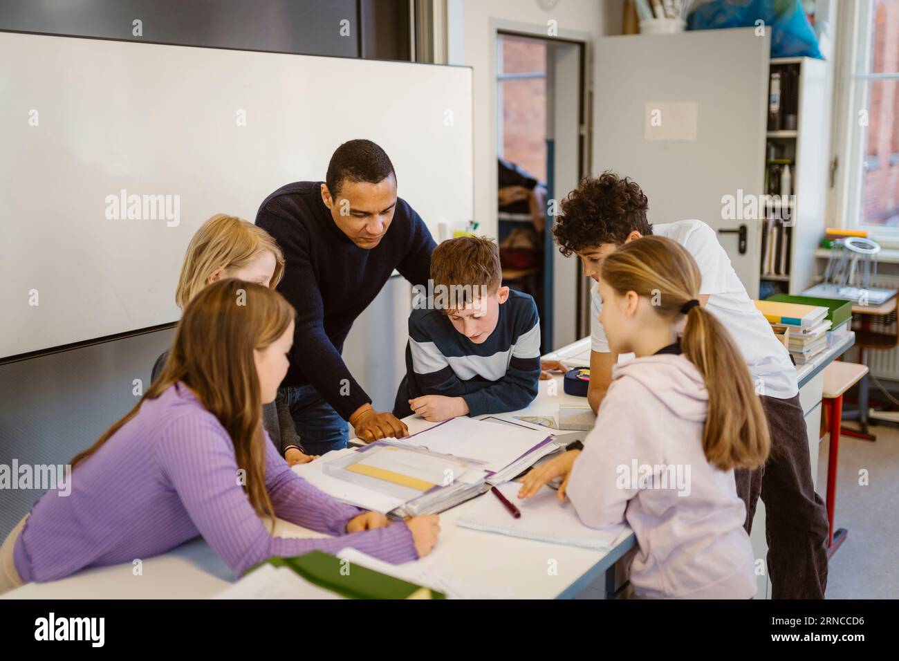 Teacher explaining male and female students leaning on desk in ...