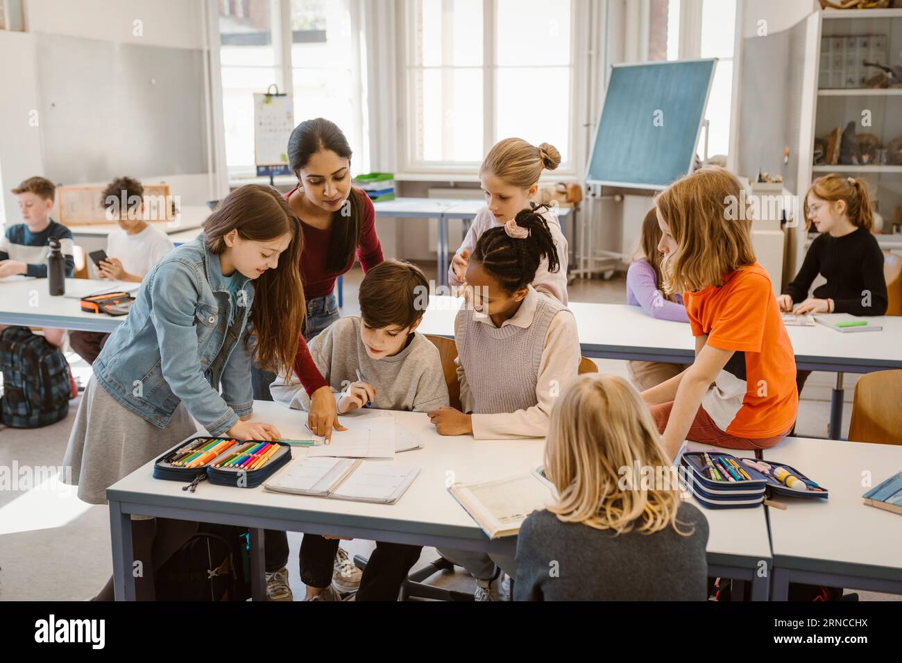 Female teacher assisting students learning together in classroom Stock ...