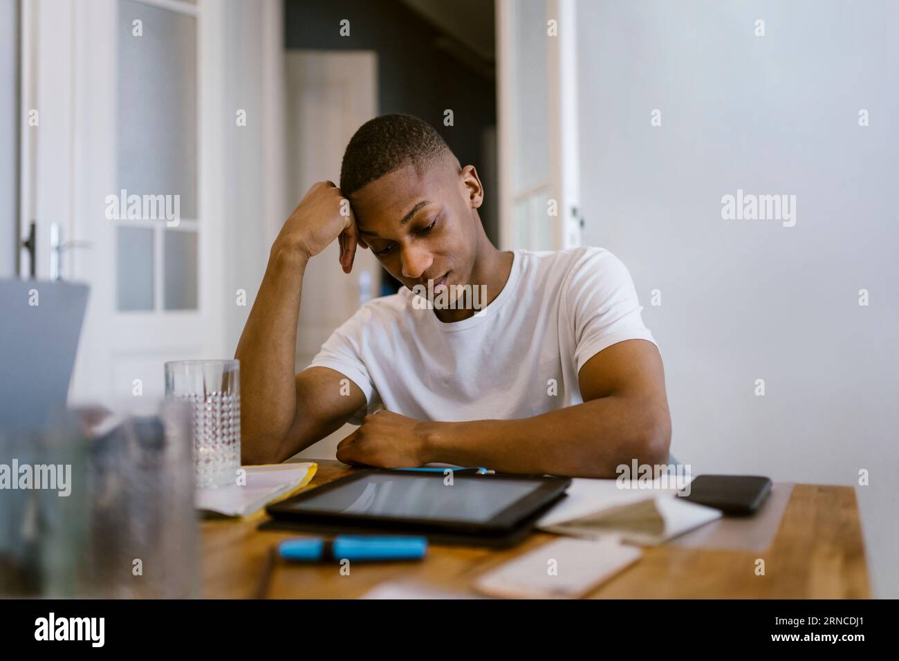 Tired young man leaning on elbow while studying at home Stock Photo - Alamy