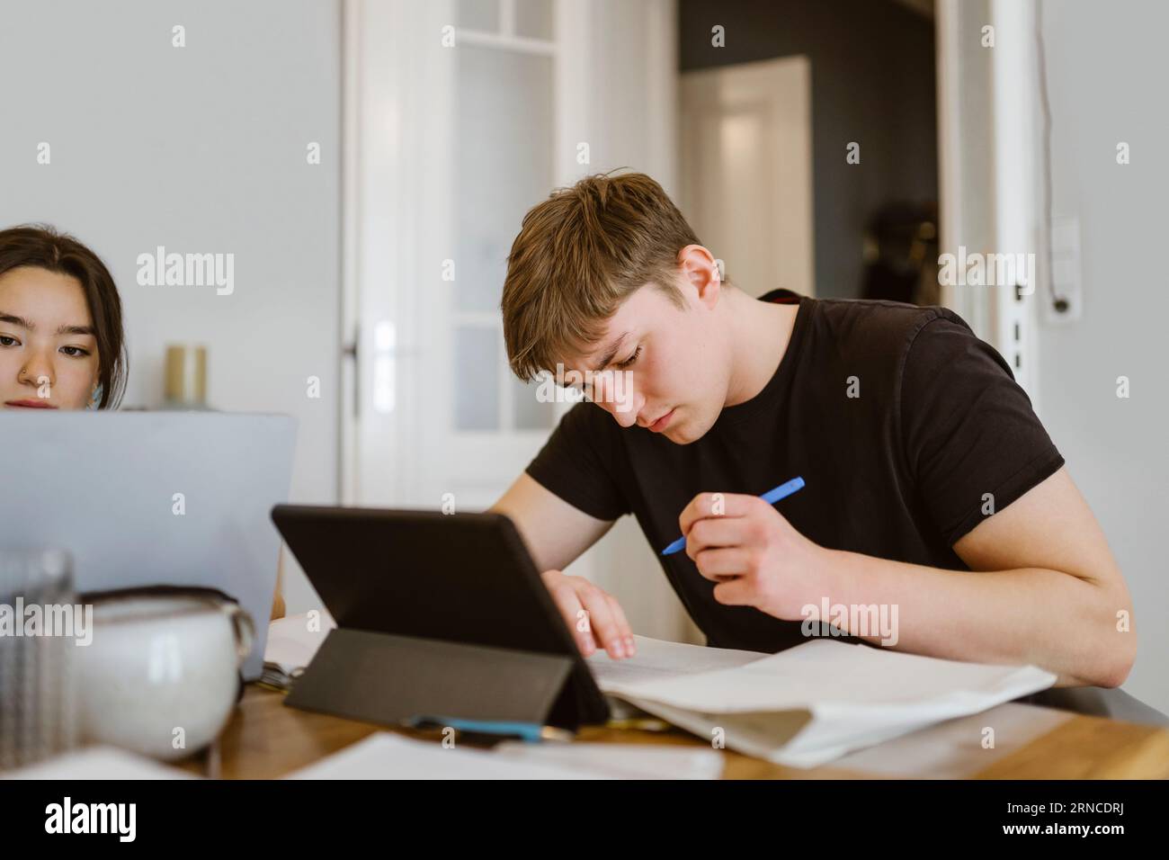Young man writing while doing homework by friend at home Stock Photo ...