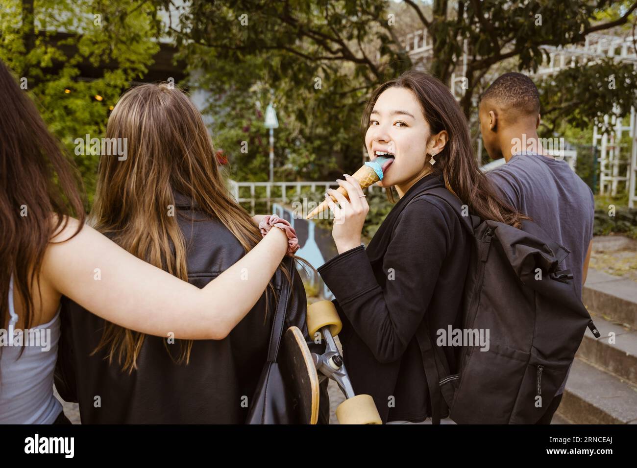 Young woman looking back while eating ice cream and walking with ...