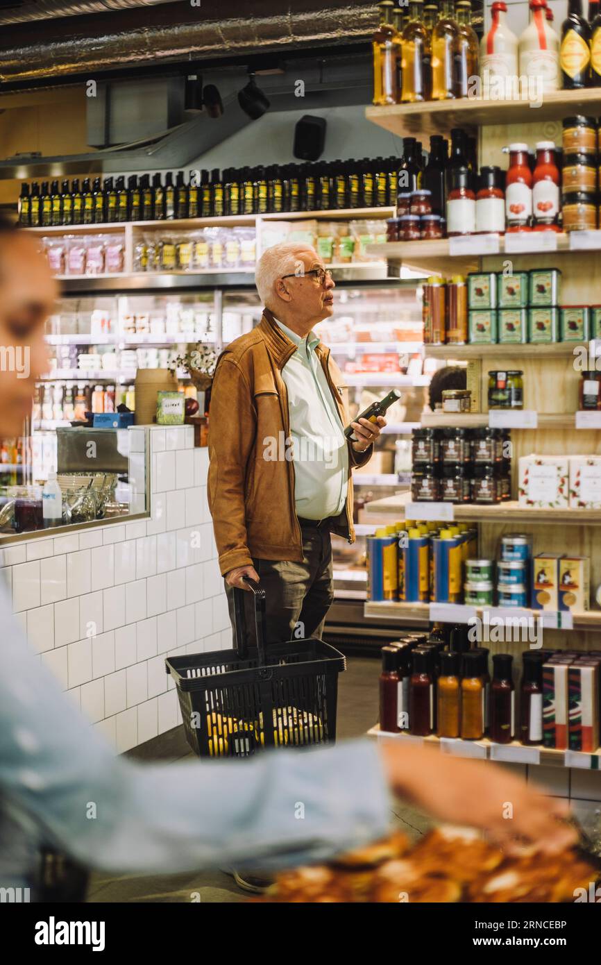 Senior man holding basket and bottle shopping at convenience store ...
