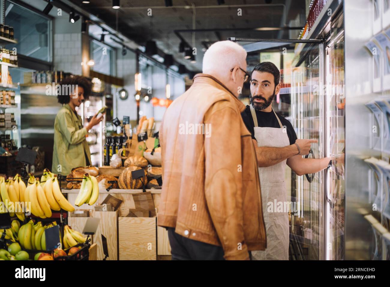 Mature retail clerk pointing while talking with senior male customer at ...