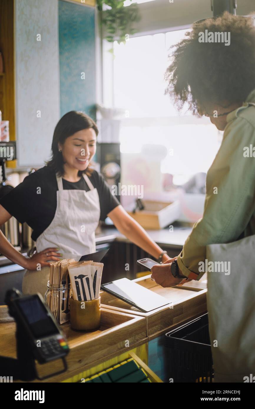 Smiling female sales clerk standing near male customer using mobile ...