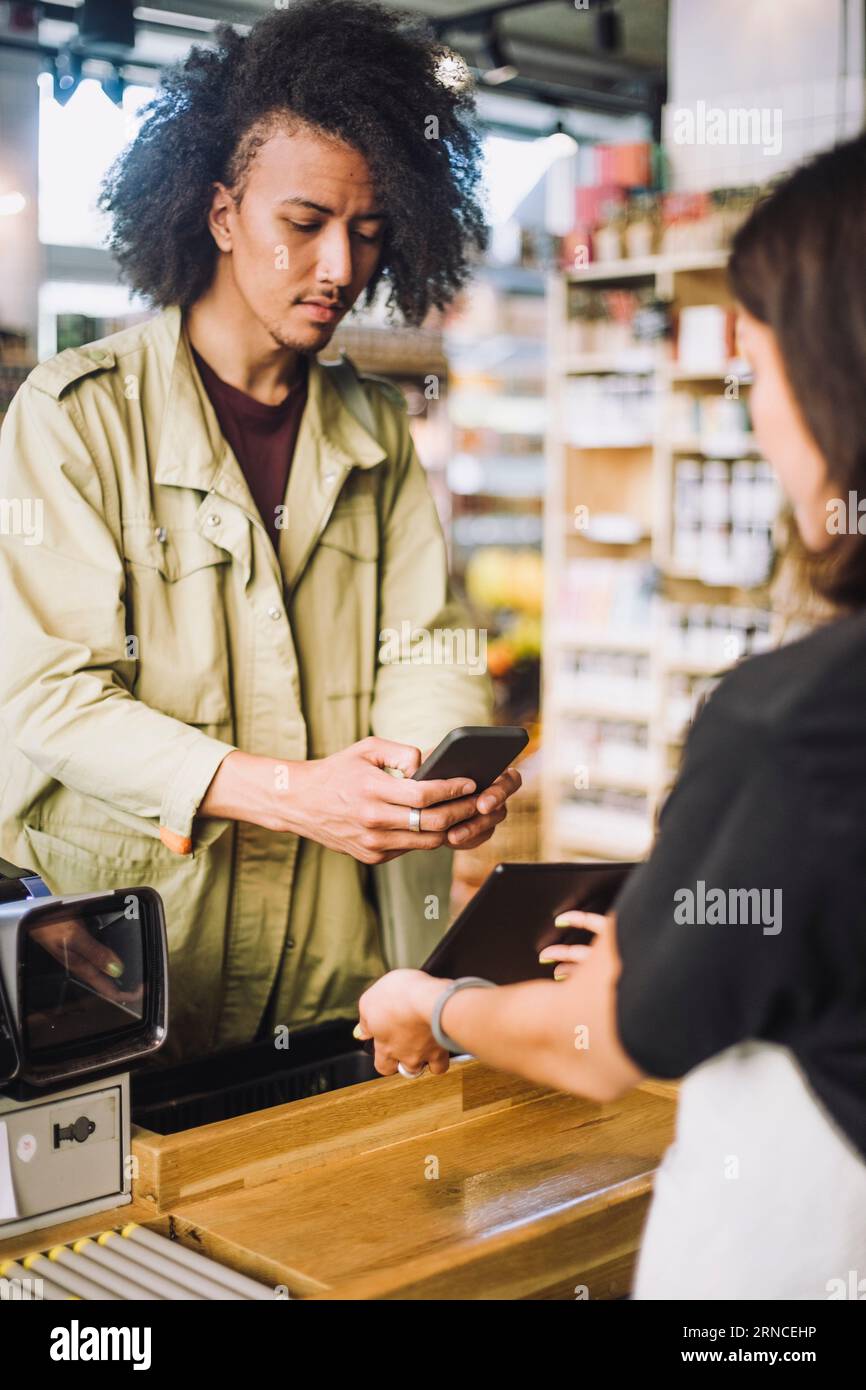 Young male customer scanning through smart phone while paying at ...