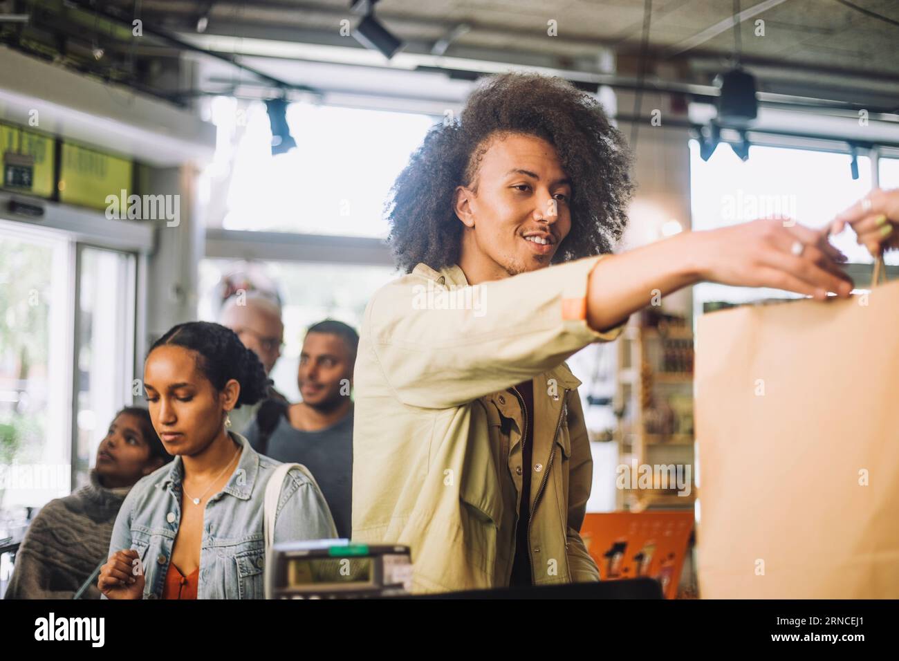Young man taking shopping bag while female customer waiting in line at ...