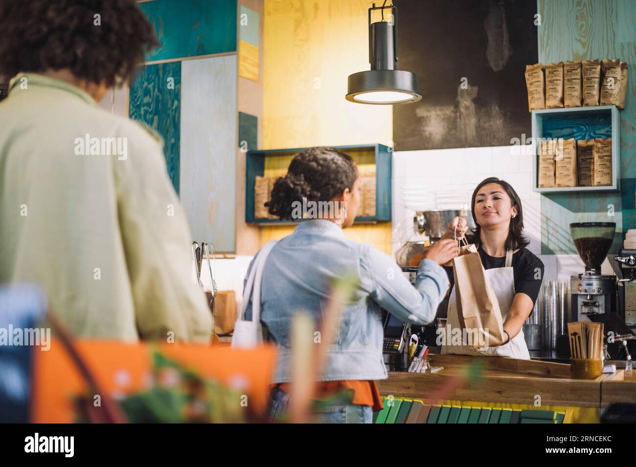 Saleswoman giving shopping bag to female customer while man waiting in ...