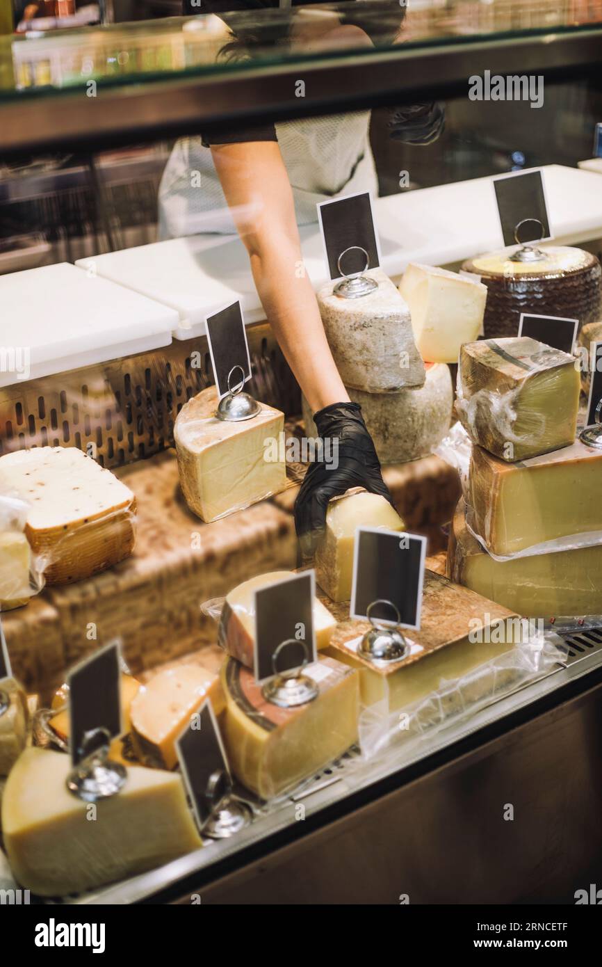 Midsection of female retail clerk removing cheese from display cabinet ...