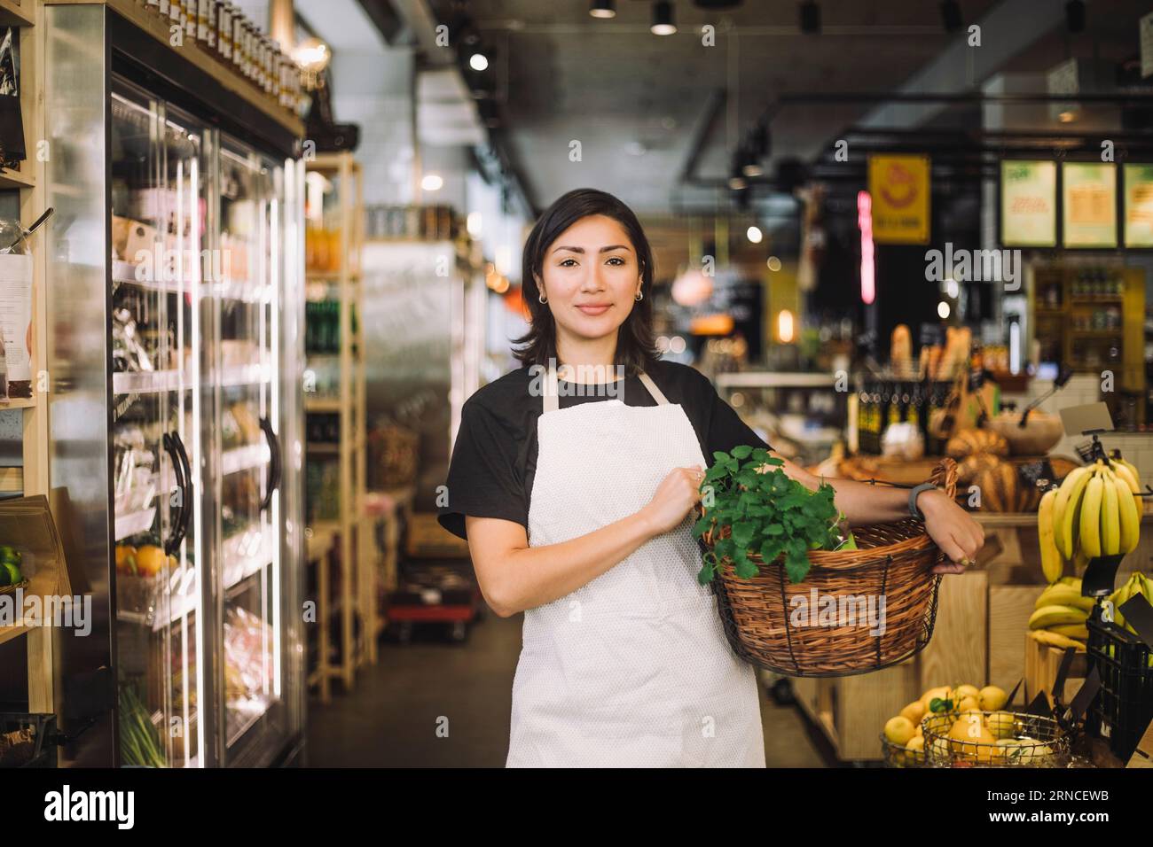 Portrait of female retail clerk carrying wicker basket while standing ...