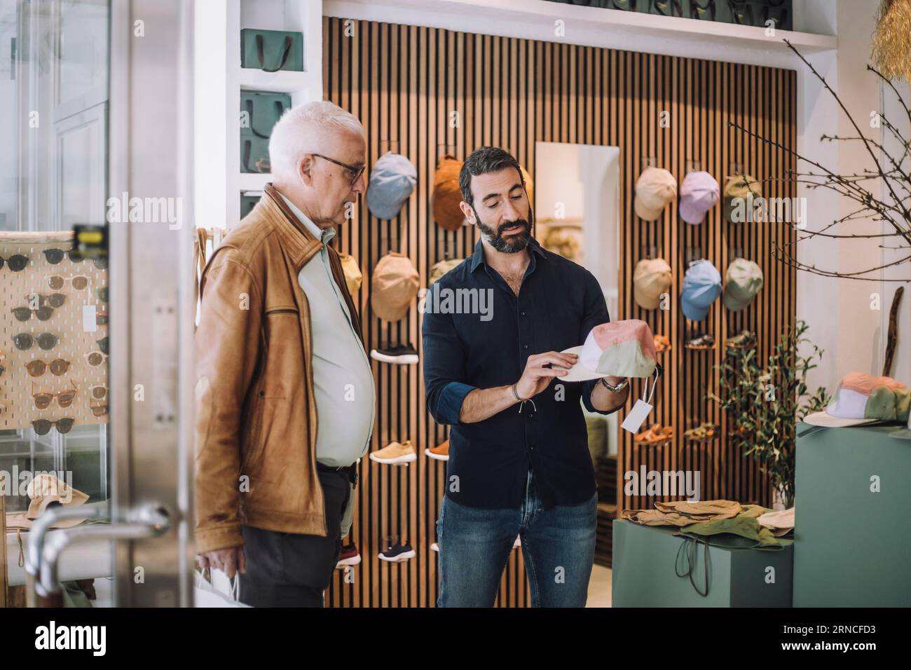 Salesman showing cap to senior male customer at clothing store Stock ...