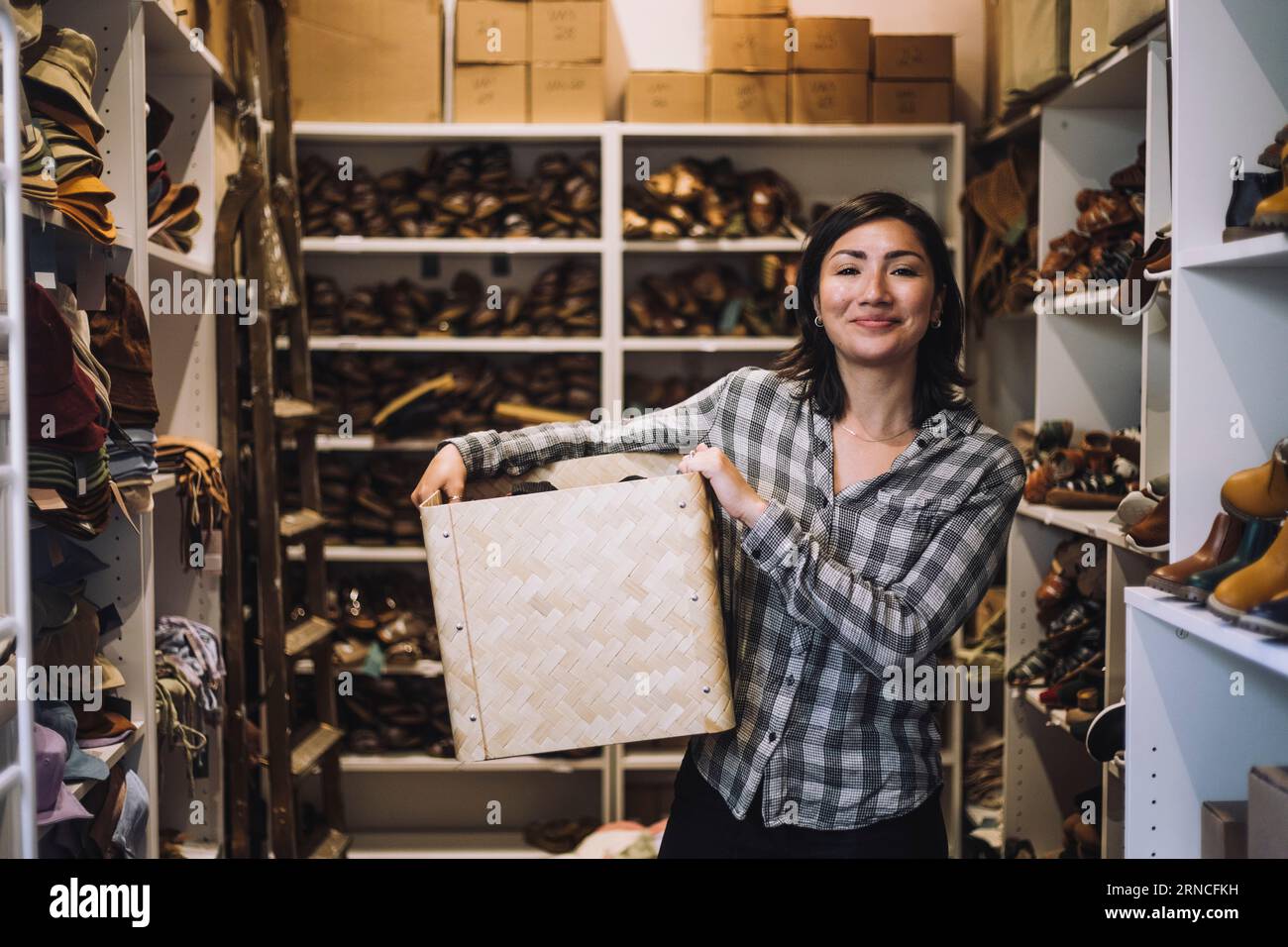 Portrait of smiling female clerk carrying wicker basket while standing ...