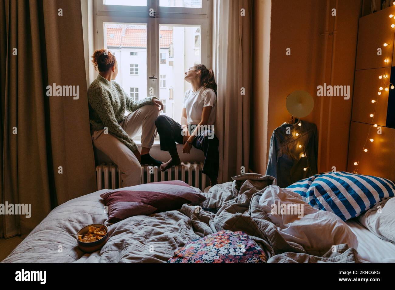 Young female friends sitting at window in bedroom Stock Photo - Alamy