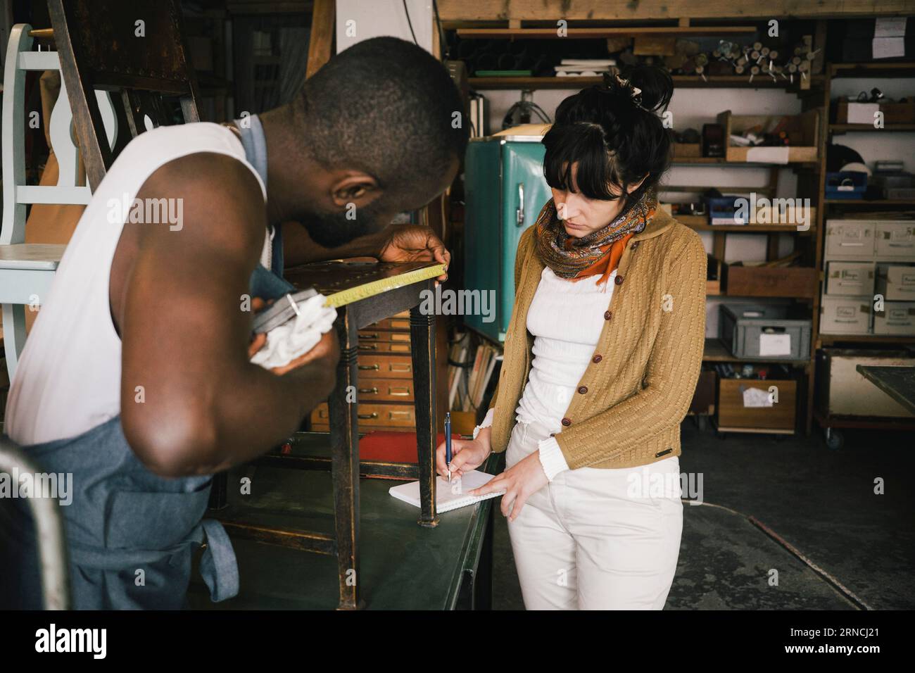 Male entrepreneur measuring chair while customer writing in diary at workshop Stock Photo - Alamy
