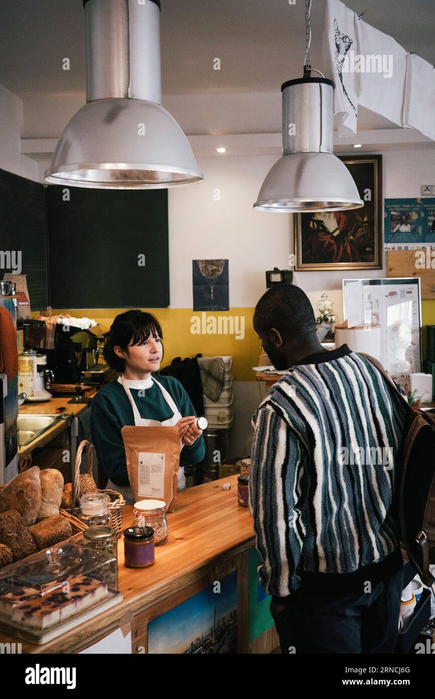 Entrepreneur talking with customer at checkout counter in food store ...