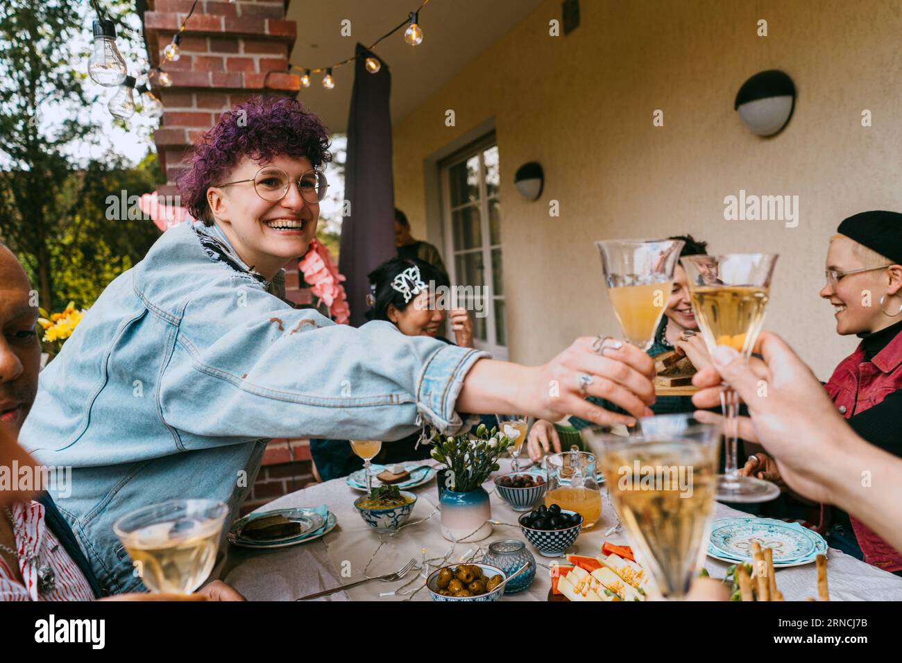 Happy non-binary person toasting drinks with friends during party in ...