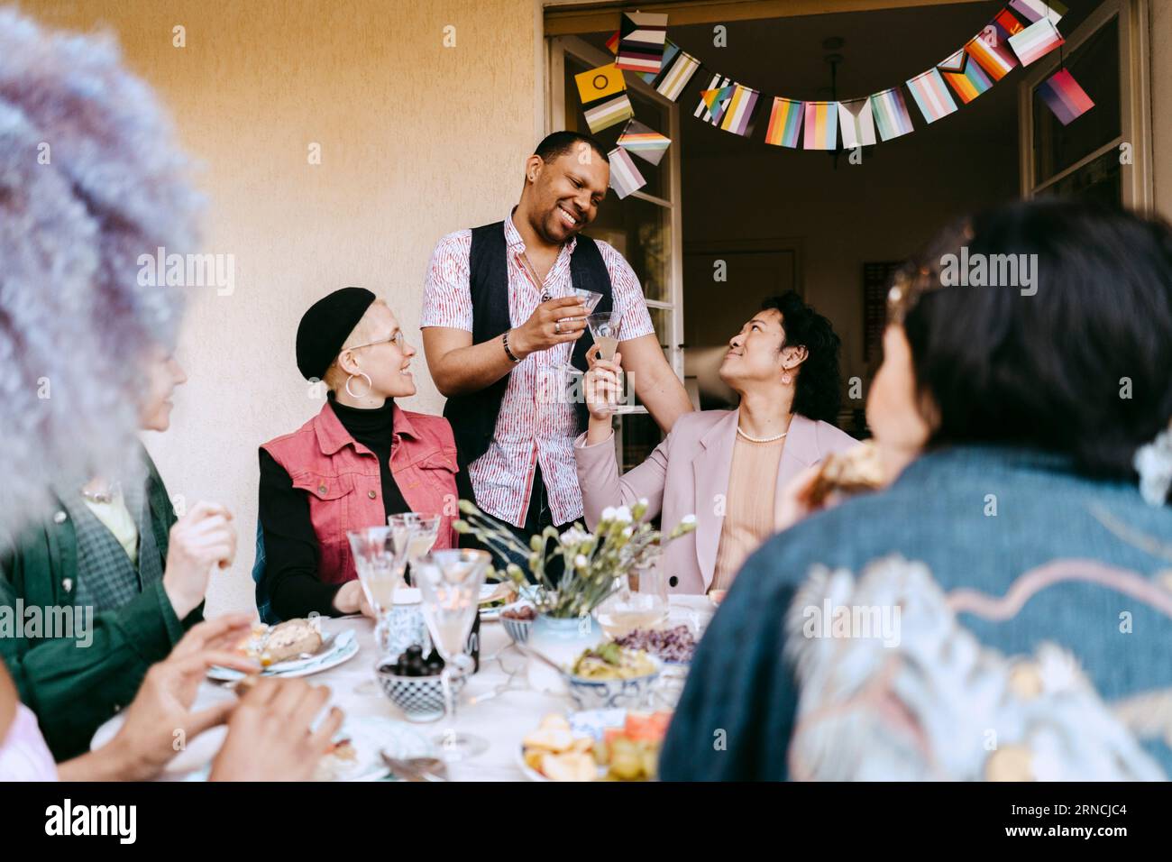 Smiling gay man enjoying drinks with LGBTQ friends during dinner party ...