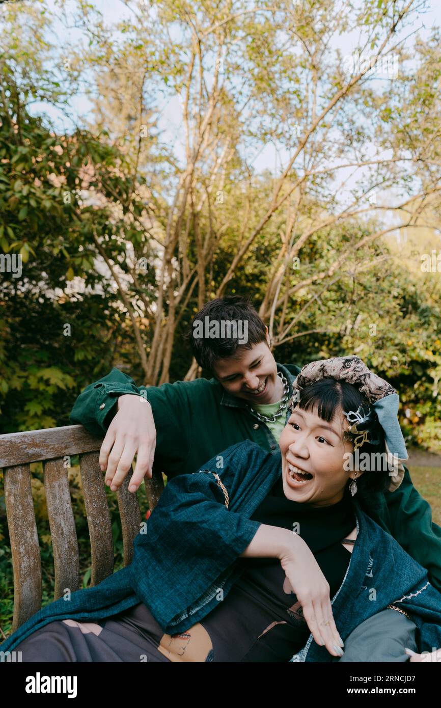 Cheerful LGBTQ friends enjoying together while sitting on bench during ...
