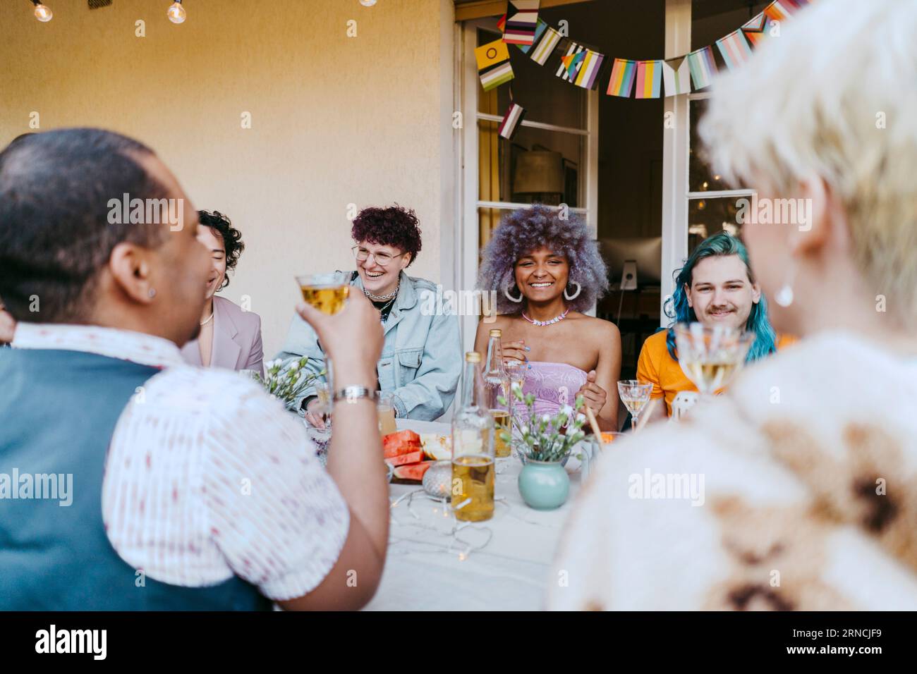 Smiling friends of LGBTQ community enjoying wine during dinner party in ...
