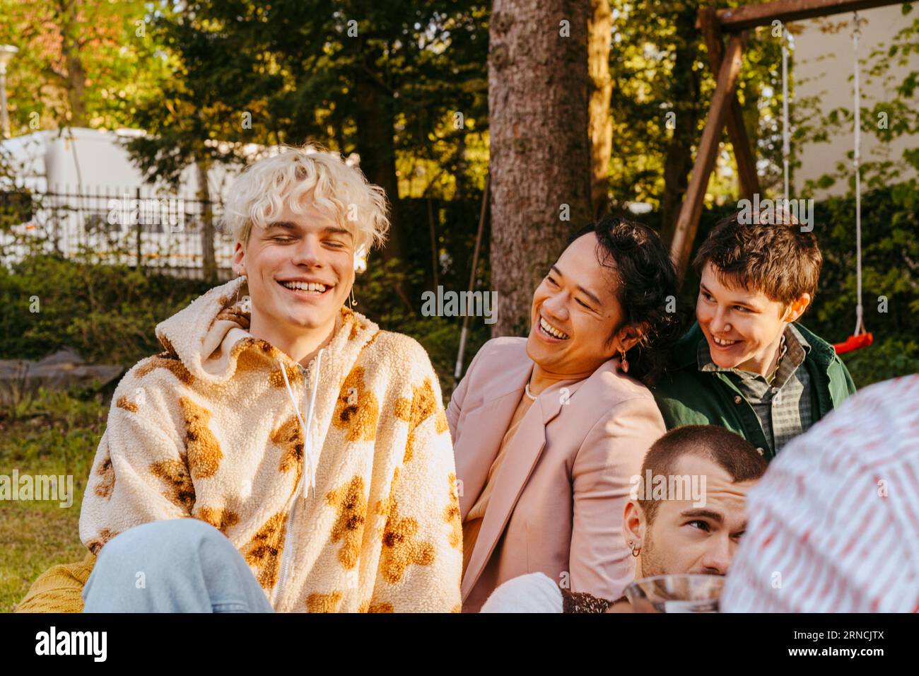 Gay Friends Laughing While Sitting Next To Each Other During Dinner Party In Back Yard Stock