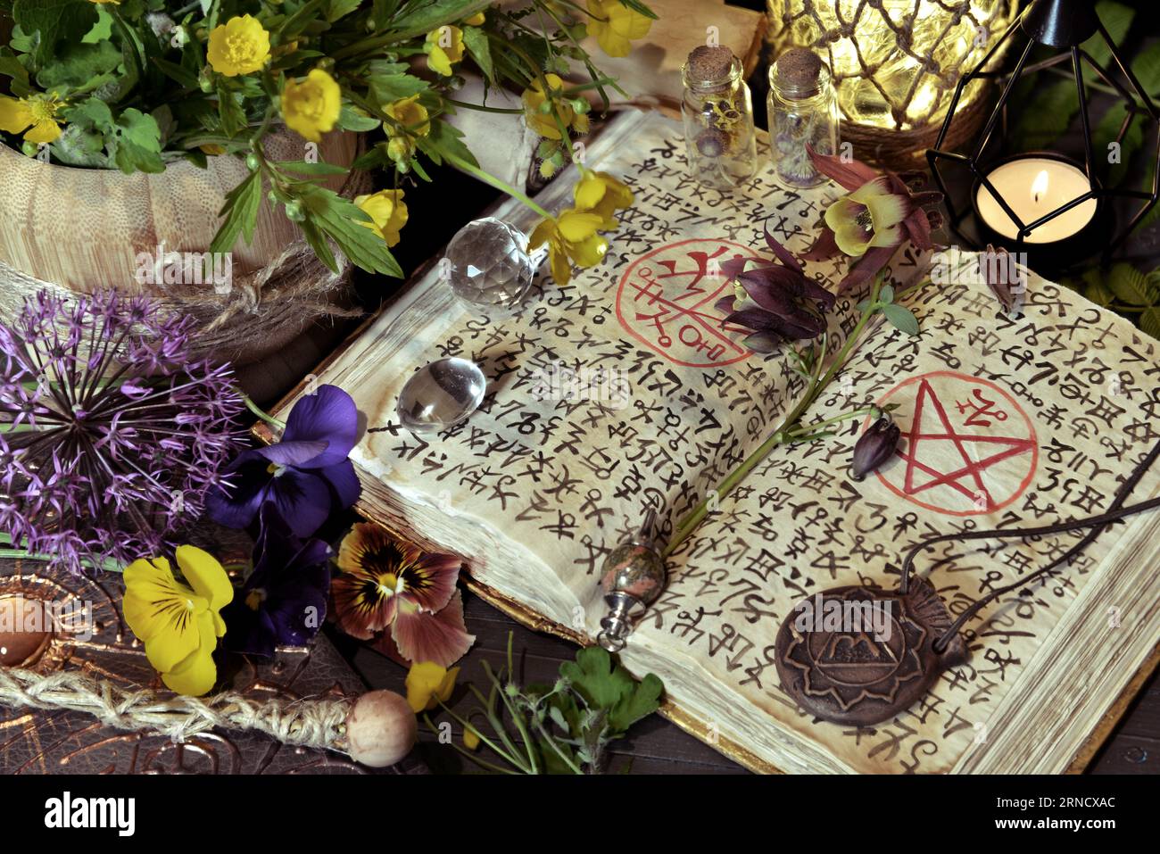 Still life with open magic book of spells, candle and medallion on ...