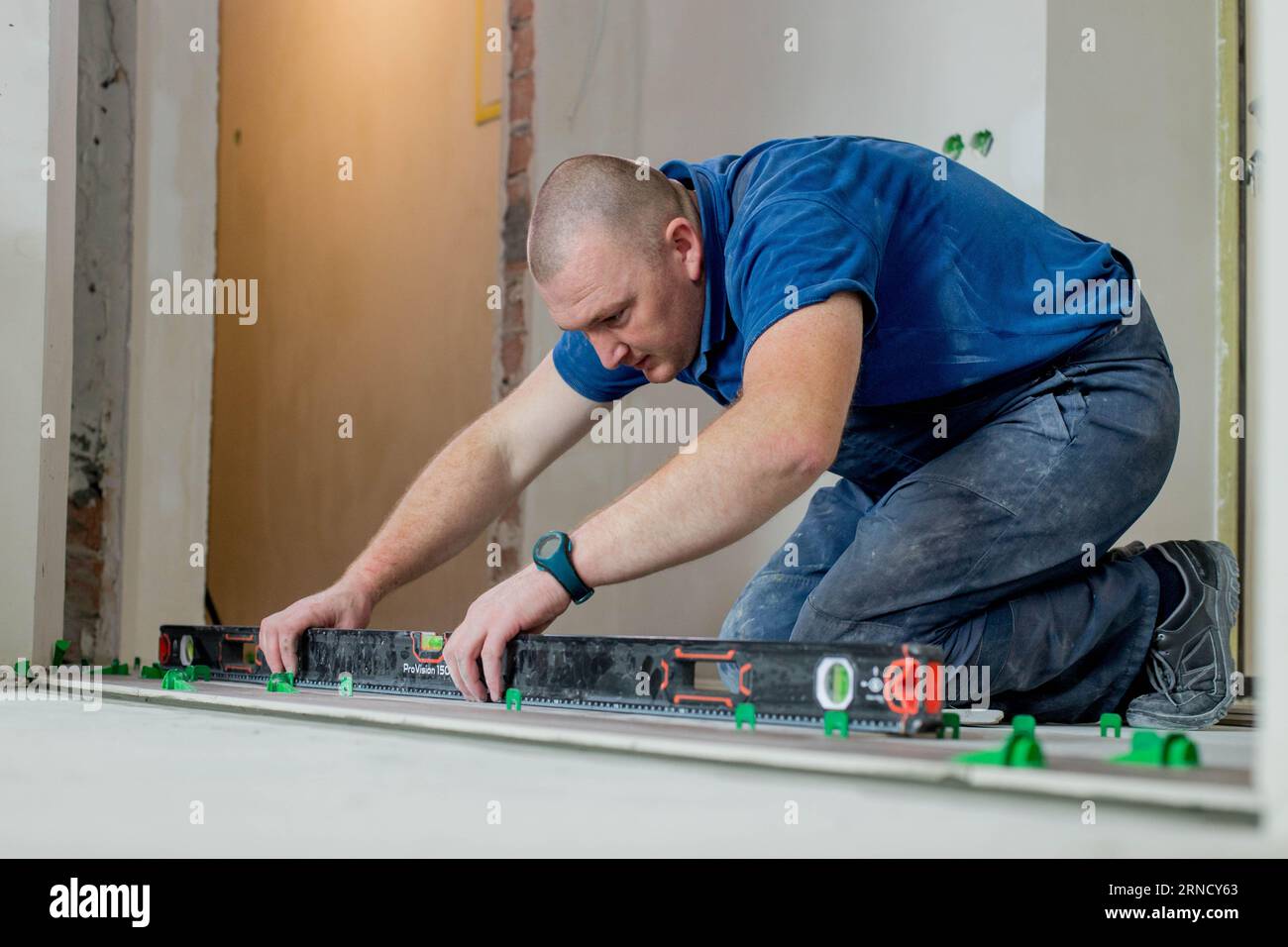 Tiler placing ceramic wall tile in position over adhesive with lash ...