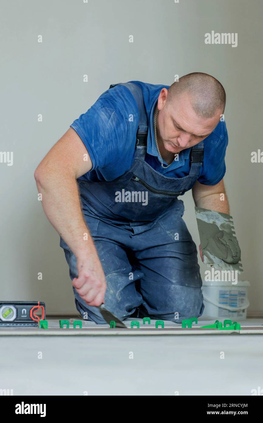 Tiler placing ceramic wall tile in position over adhesive with lash ...