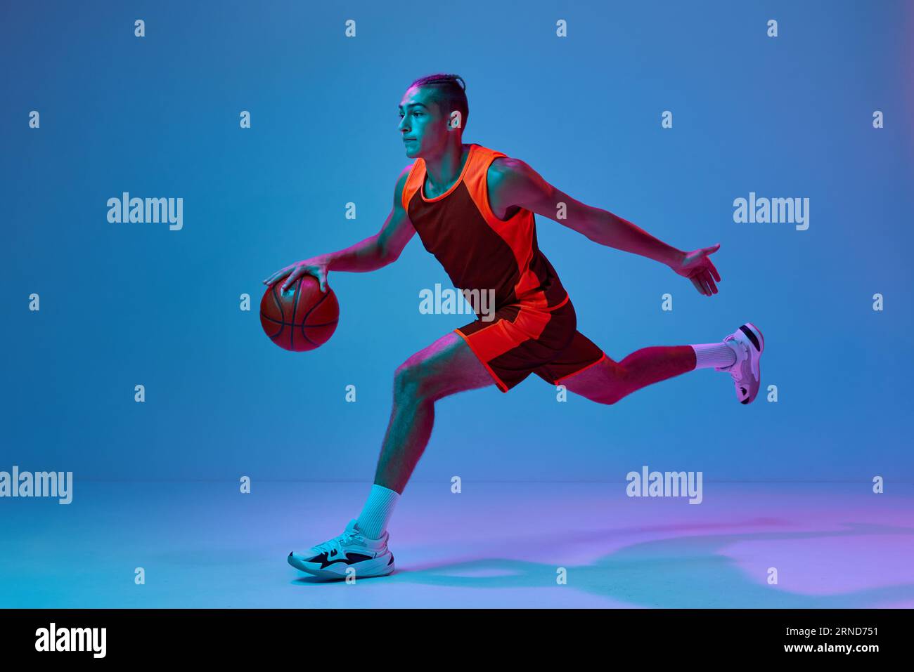 Dynamic image of teen boy in uniform, playing basketball against blue ...