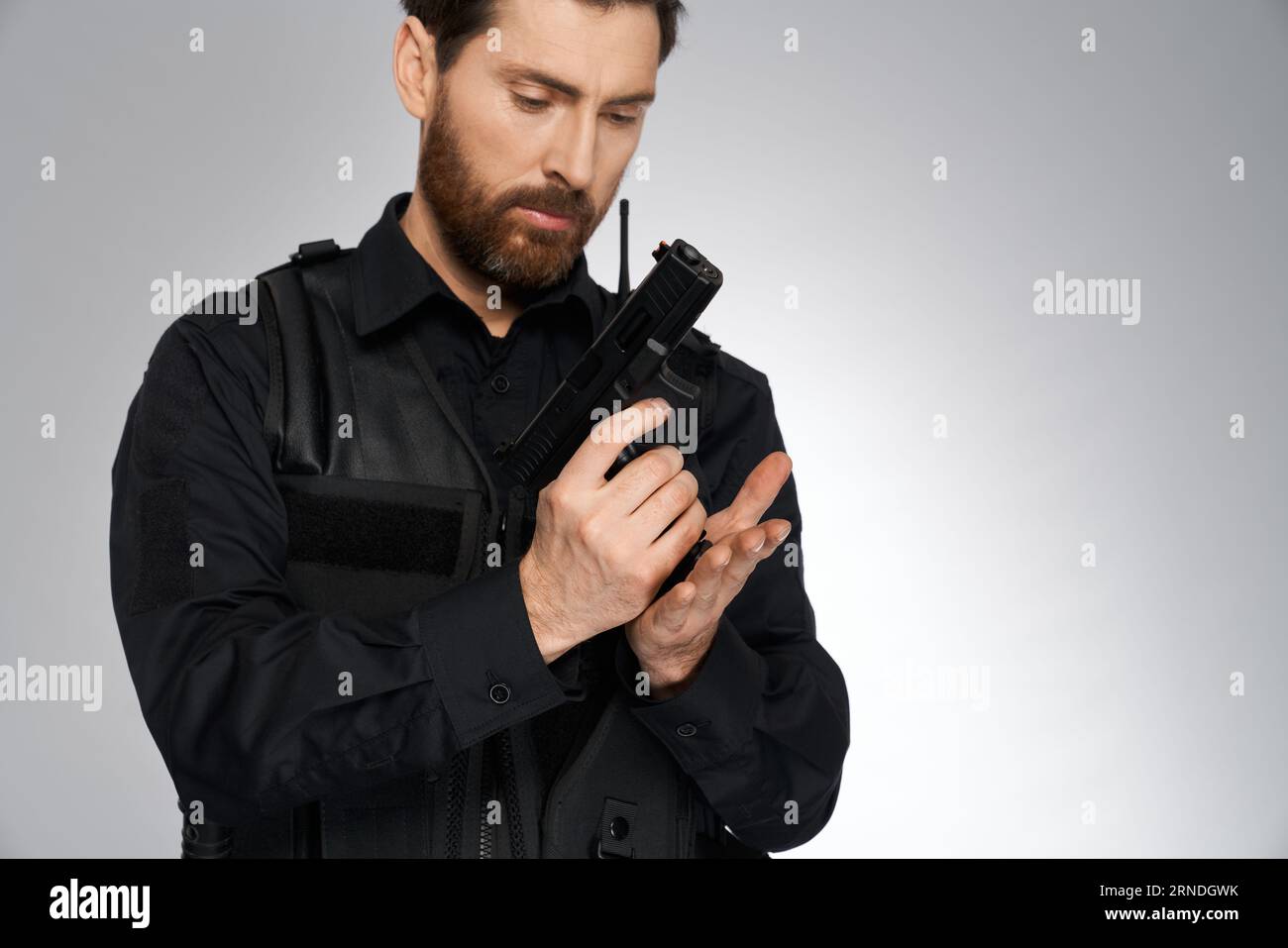 Focused dark-haired officer reloading weapon, getting ready to shoot indoors. Portrait of male ...
