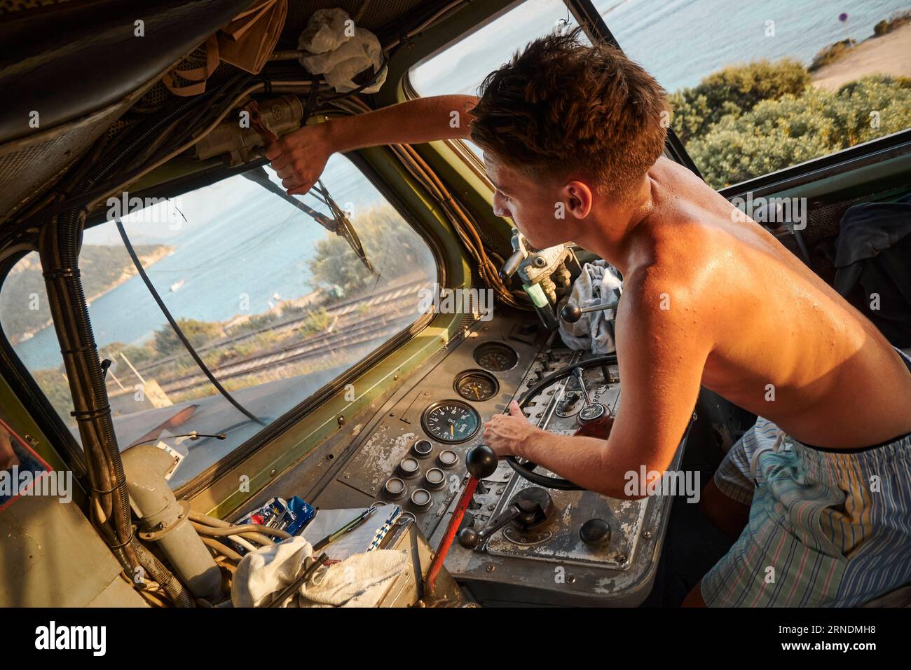 A Caucasian man in the driver's cab of a large locomotive, adjusting a ...