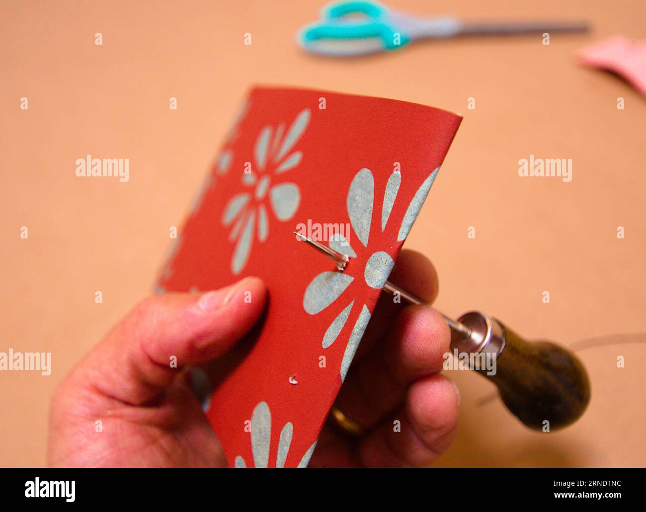 Art project in progress using paper, awl, needle, thread and scissors ...