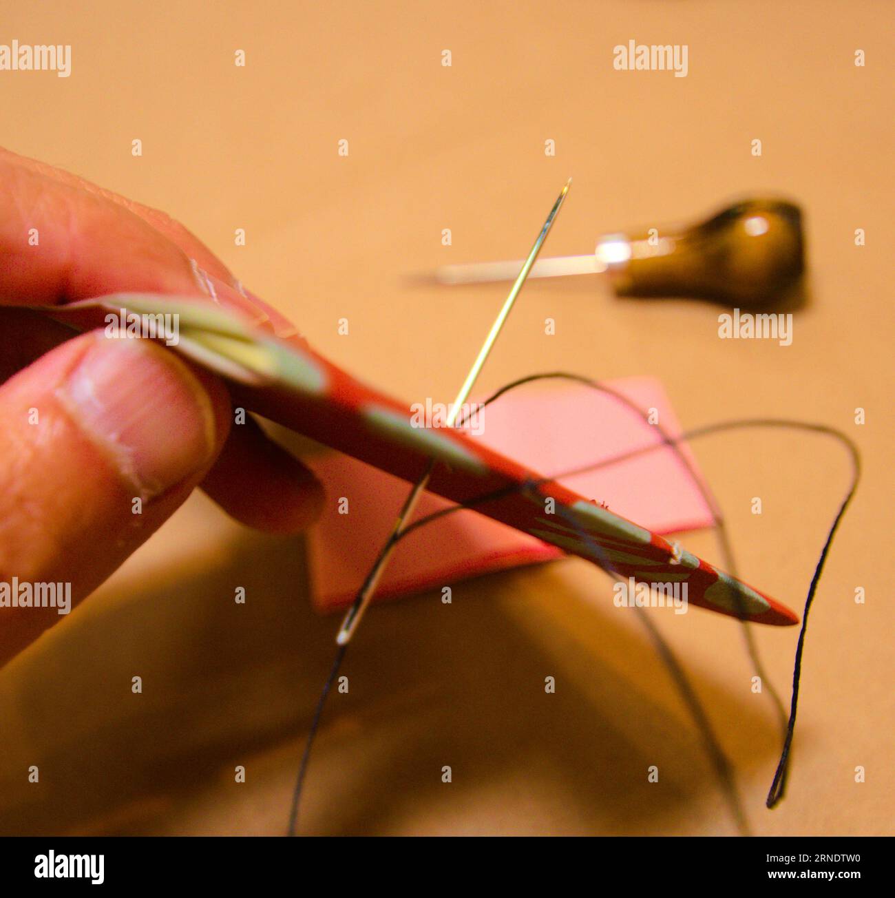 Art project in progress using paper, awl, needle, thread. A hand holds ...