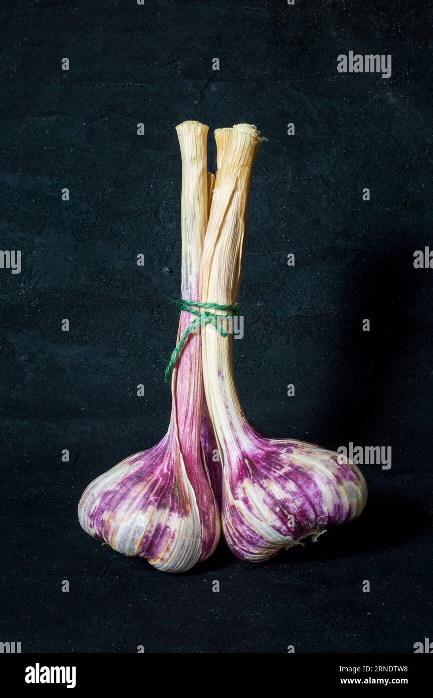 three whole purple garlic on a black background Stock Photo - Alamy
