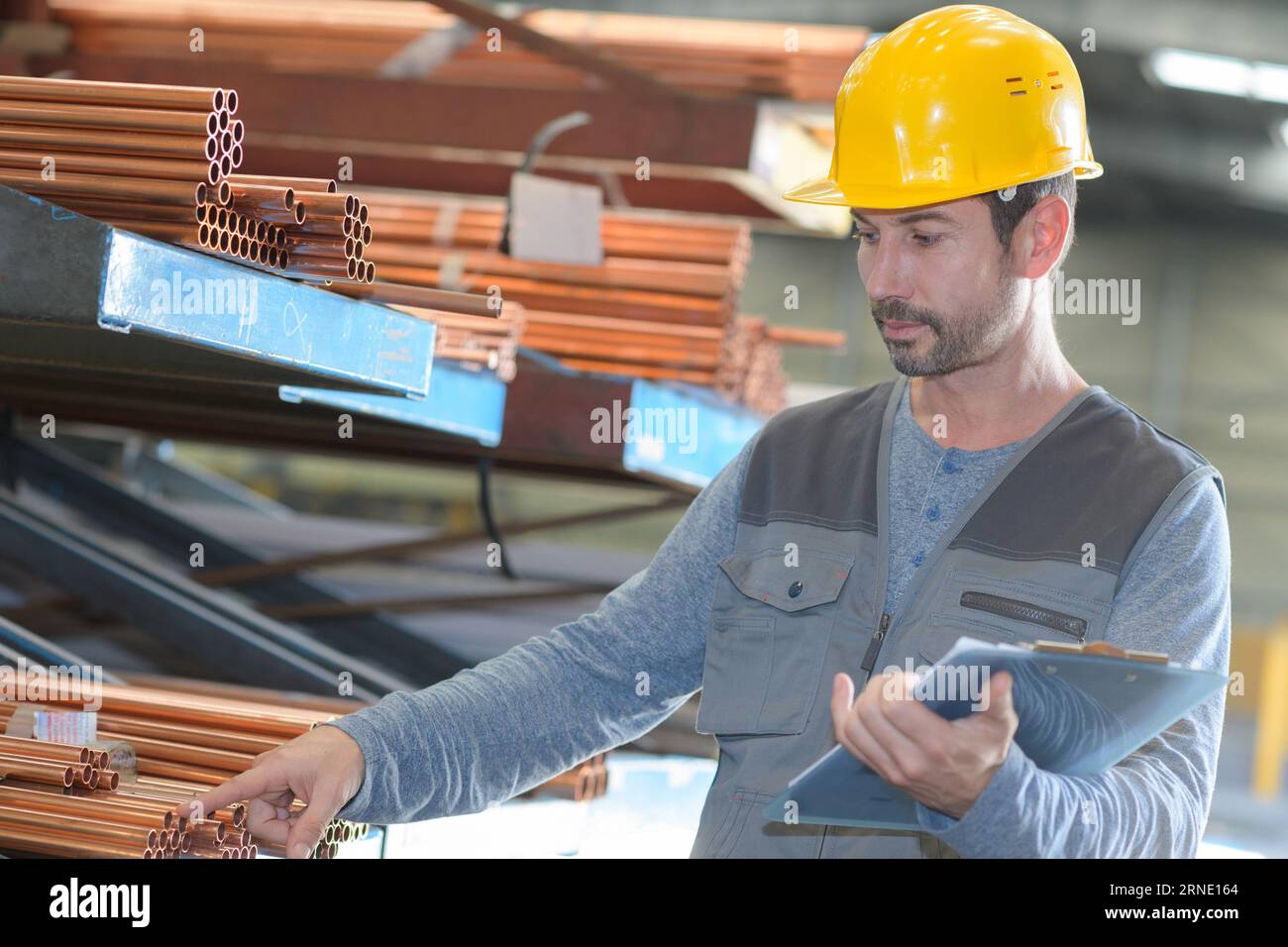 male warehouse worker with clipboard counting stock of copper pipes ...