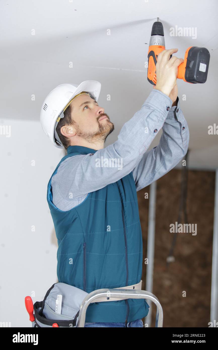 workman using a cordless drill to make hole in ceiling Stock Photo - Alamy