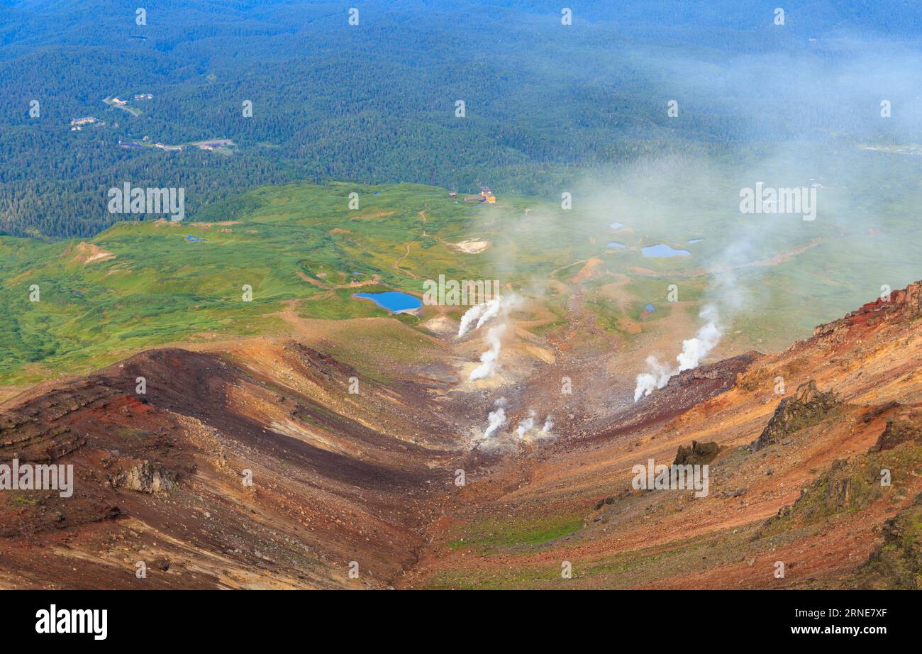 Steep volcanic slope with gas and steam vents above green meadows and ...