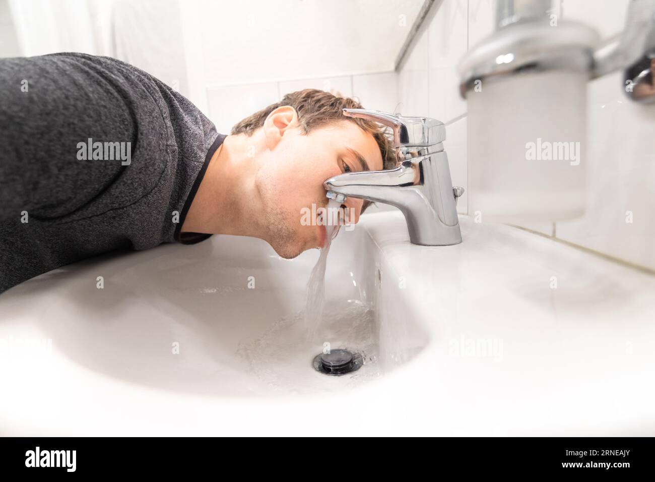 Young Man Drink Tap Water By Mouth Out Of Sink In Bathroom With Lips And Tongue In Flowing Water