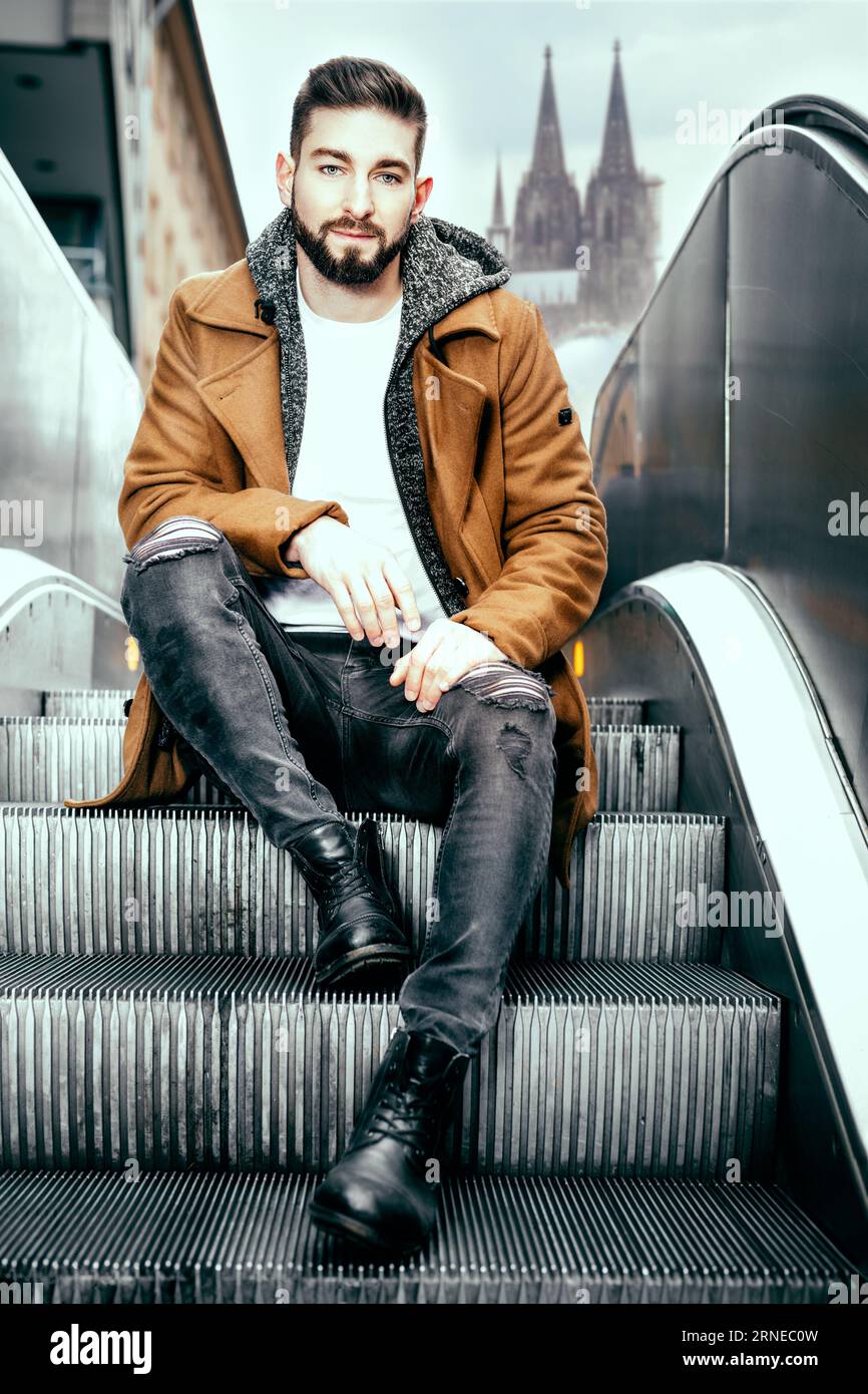 man sit on moving stair on his way up from underground to city while ...