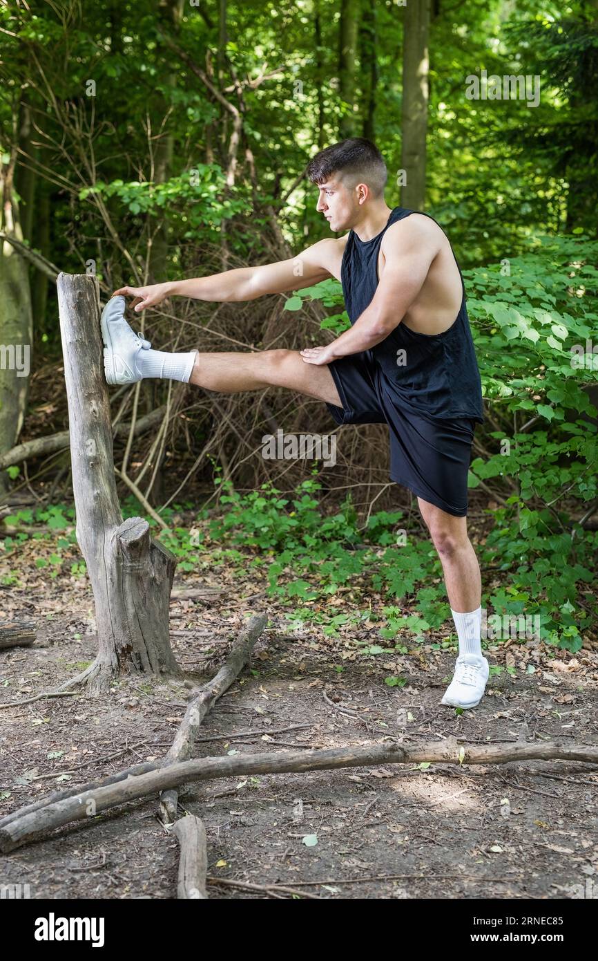 sportive and athletic fitness guy do some leg stretching in the forrest ...