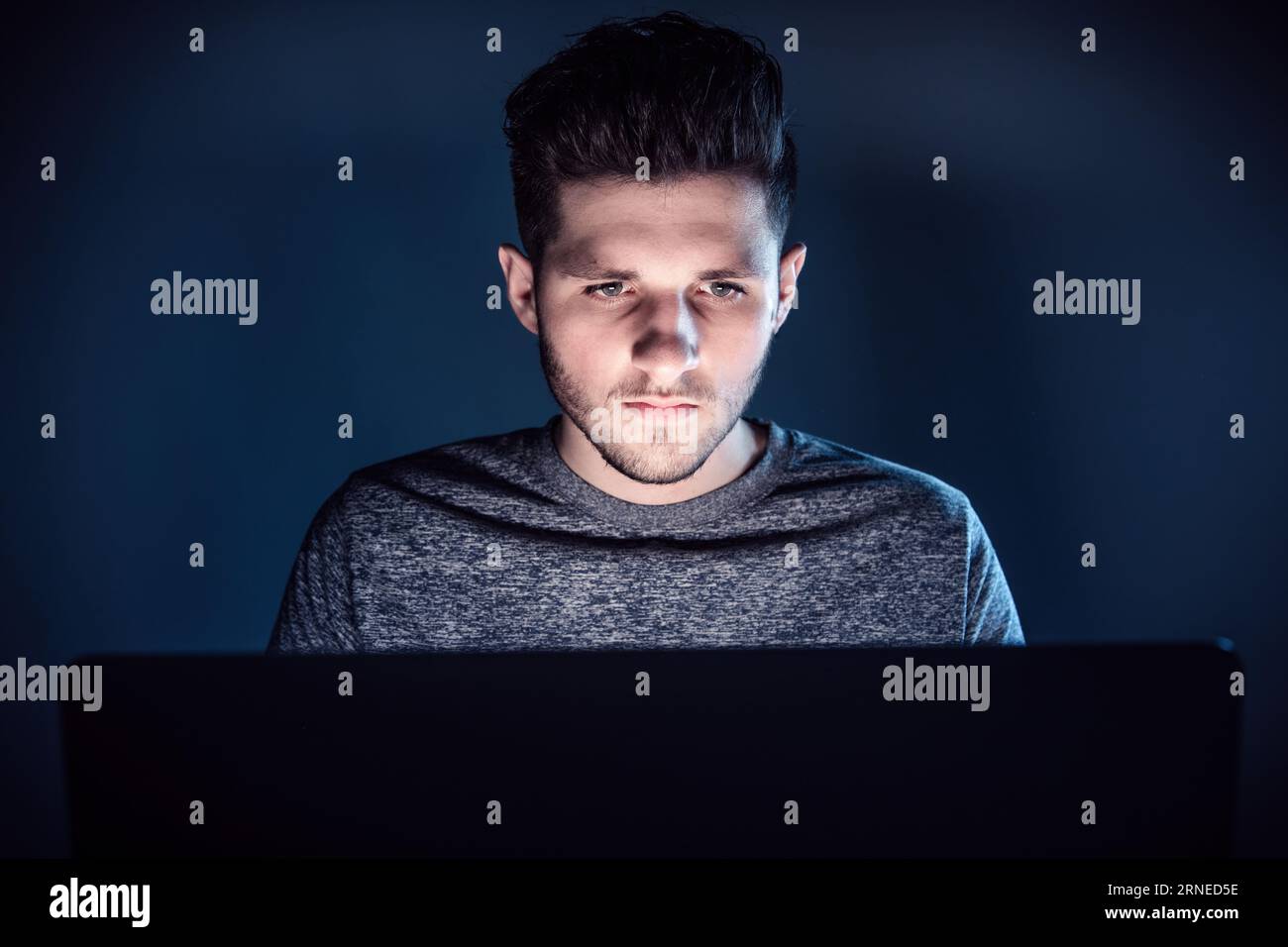 man at night in front of laptop look to screen with serious face while ...